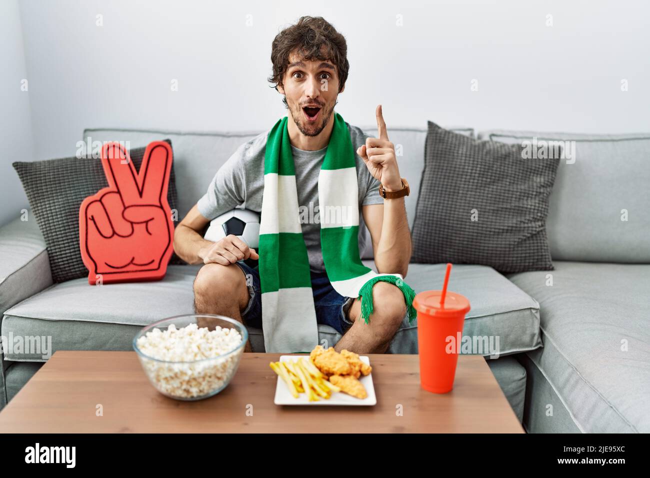 Young hispanic man football hooligan cheering game at home pointing ...
