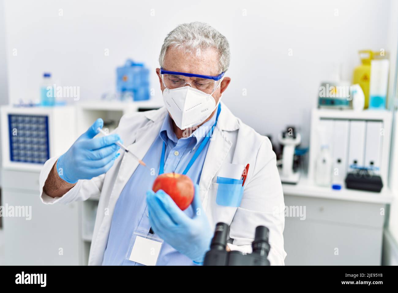 Middle age grey-haired man wearing scientist uniform holding syringe ...