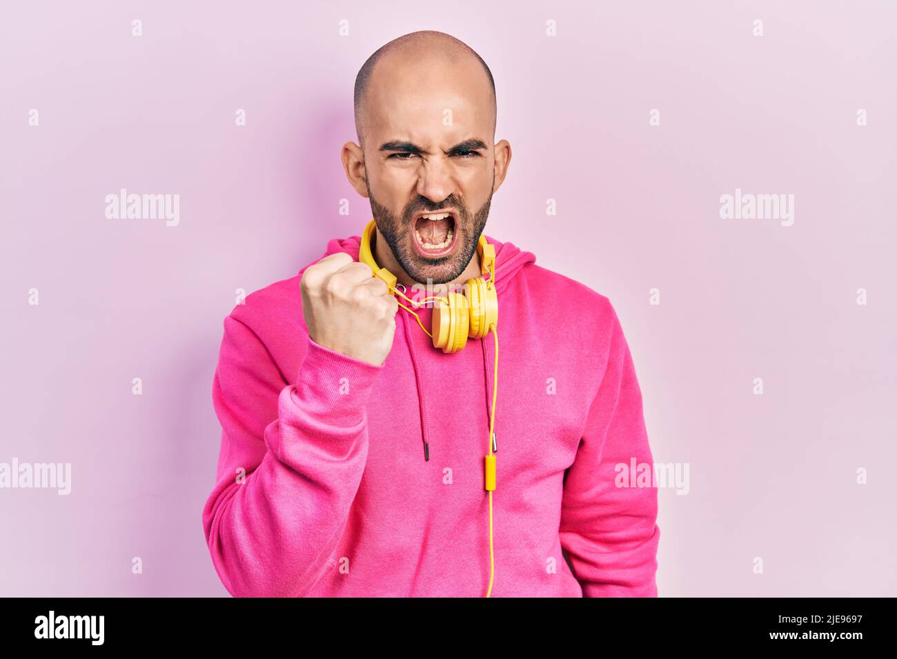 Young bald man wearing gym clothes and using headphones angry and mad ...