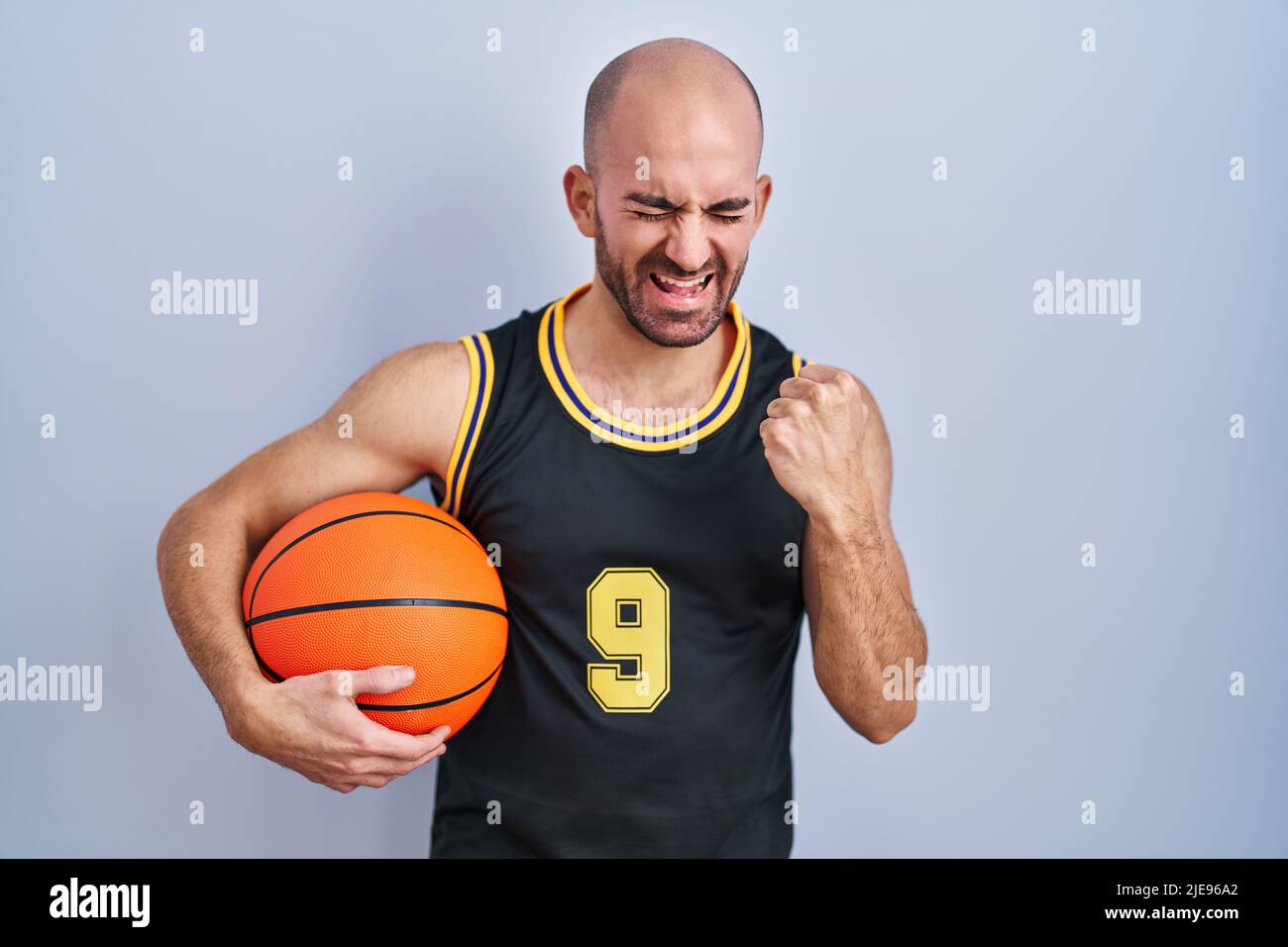 Young bald man with beard wearing basketball uniform holding ball very ...