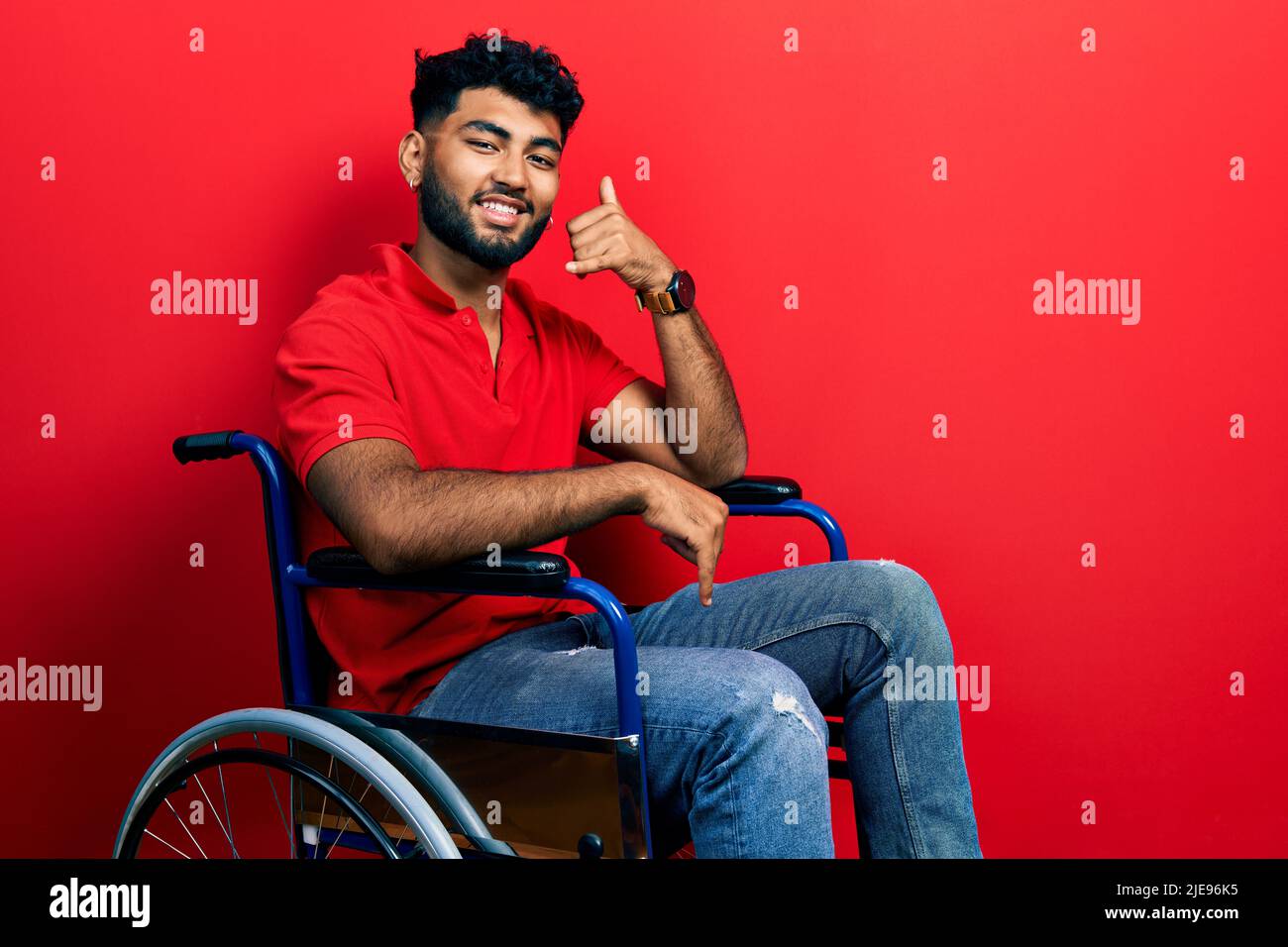 Arab man with beard sitting on wheelchair smiling doing phone gesture ...