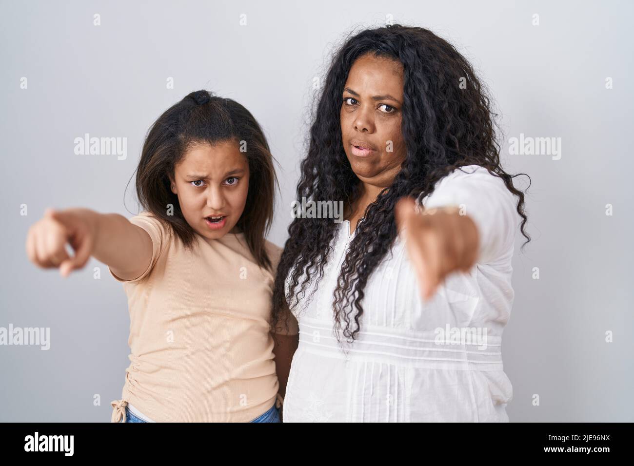 Mother and young daughter standing over white background pointing ...