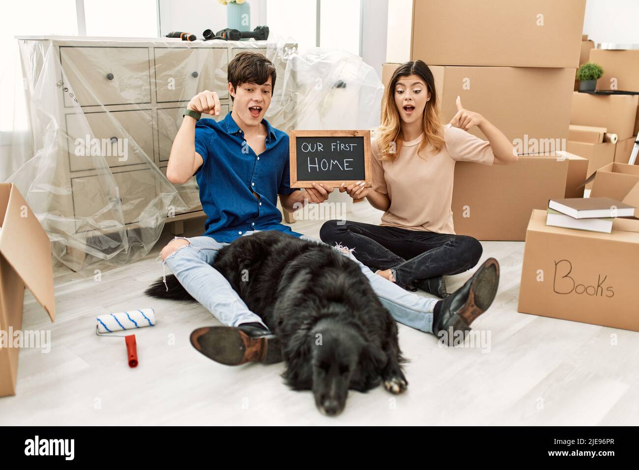 Young caucasian couple with dog holding our first home blackboard at ...