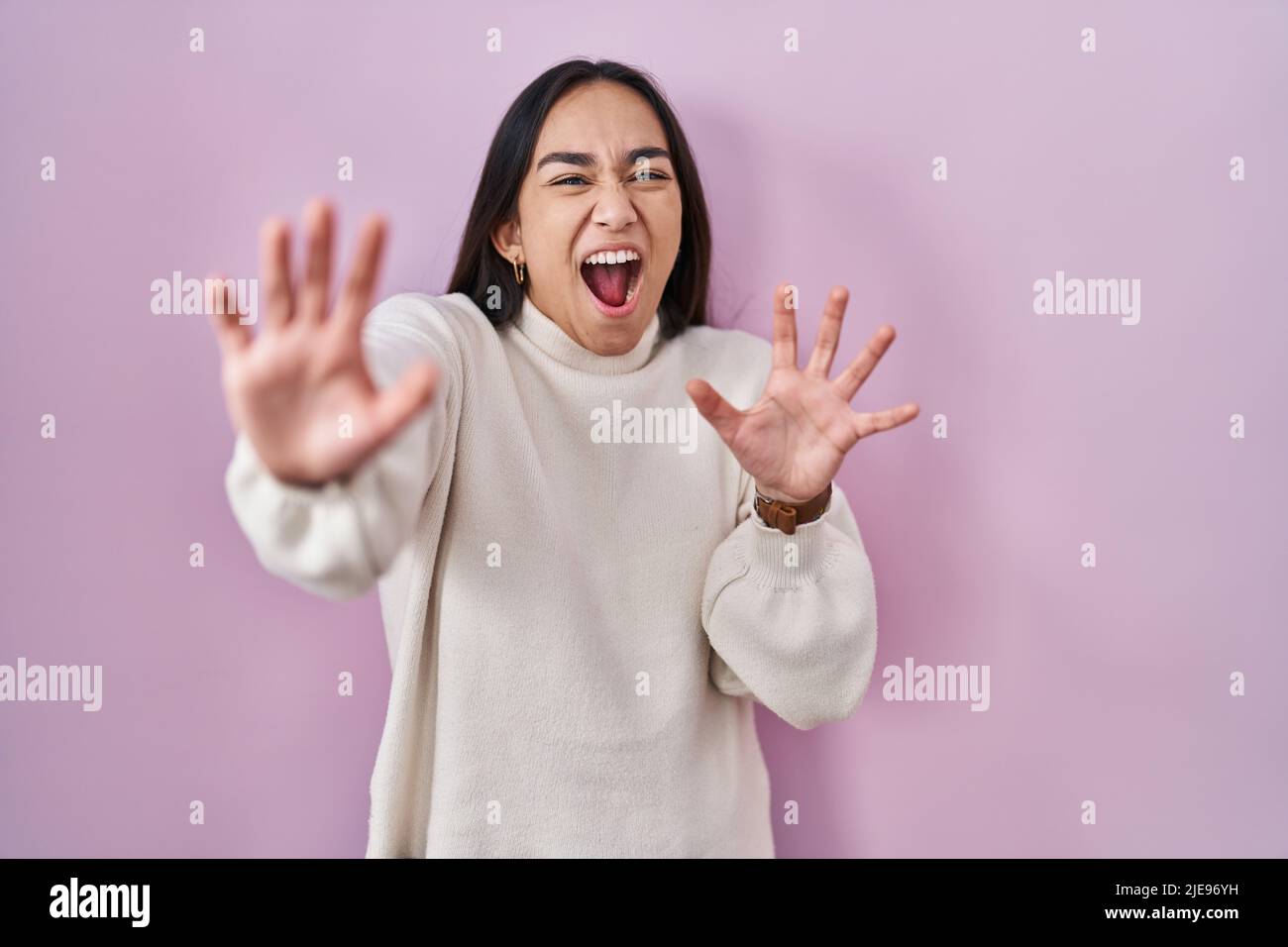 Young south asian woman standing over pink background afraid and ...