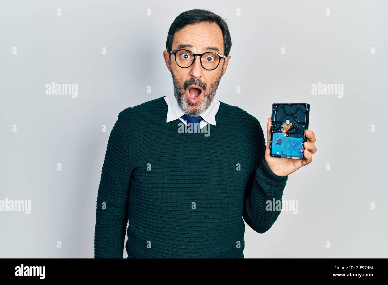 Middle age hispanic man holding hdd disk scared and amazed with open ...