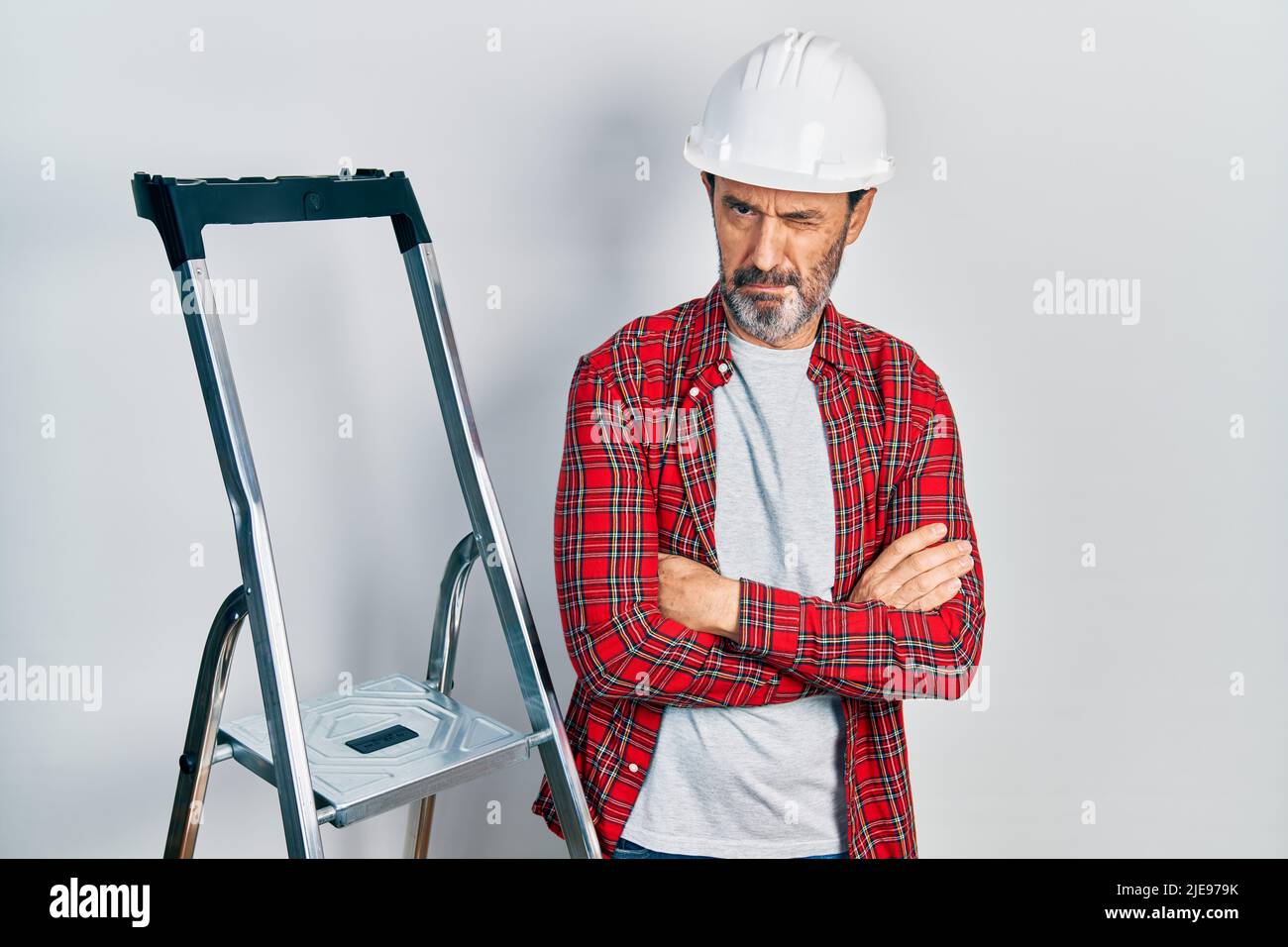 Middle age hispanic worker man with arms crossed gesture using ladder ...
