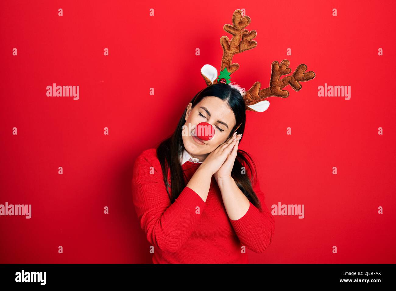 Young hispanic woman wearing deer christmas hat and red nose sleeping ...