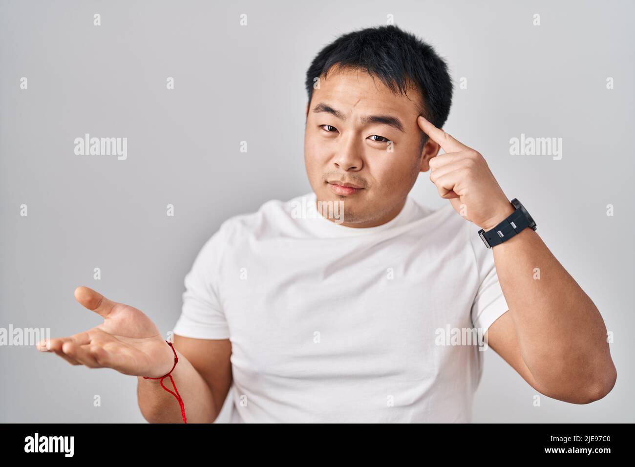 Young chinese man standing over white background confused and annoyed ...
