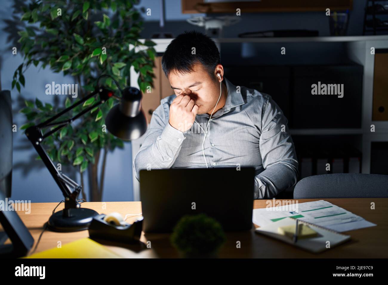 Young chinese man working using computer laptop at night tired rubbing ...