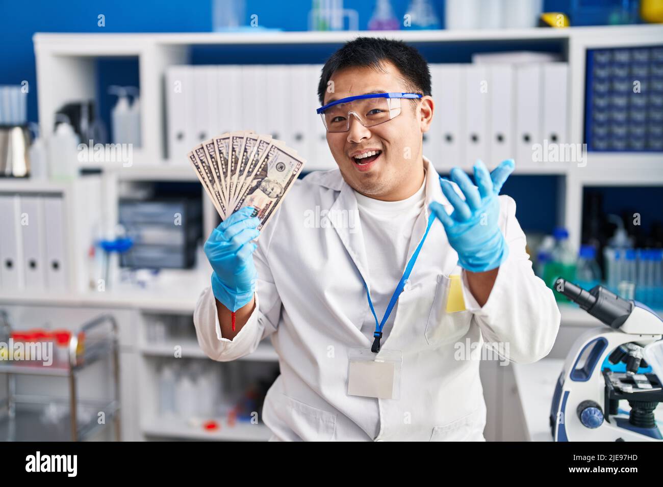 Young chinese man working at scientist laboratory holding money ...