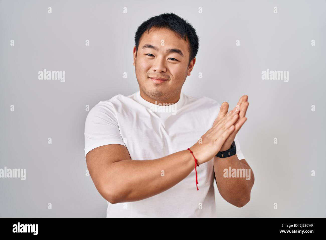 Young chinese man standing over white background clapping and ... Young chinese man standing over white background clapping and ...