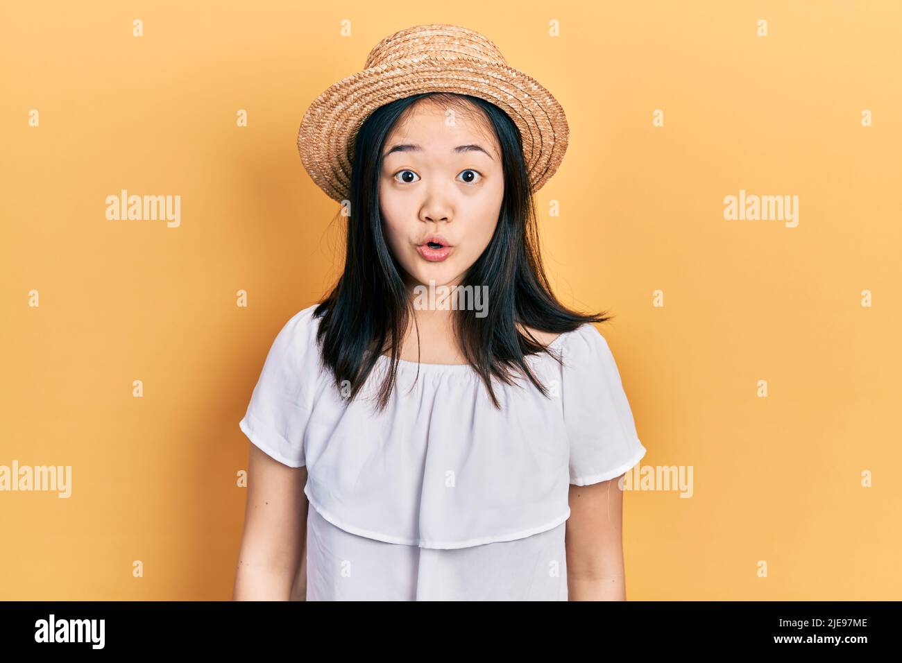 Young chinese girl wearing summer hat scared and amazed with open mouth ...