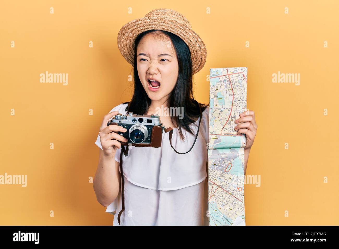 Young chinese girl holding city map and vintage camera angry and mad ...