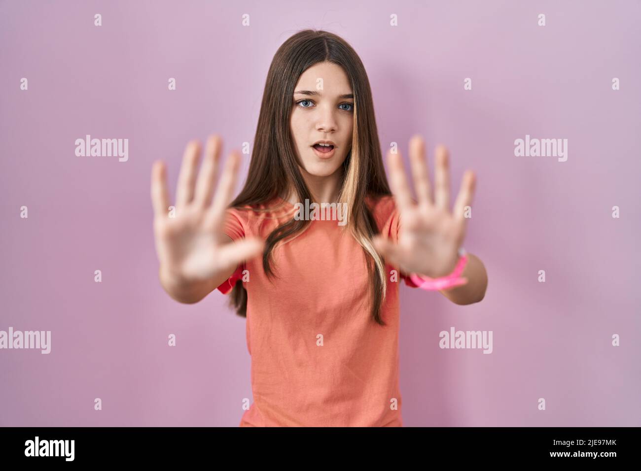 Teenager girl standing over pink background doing stop gesture with ...
