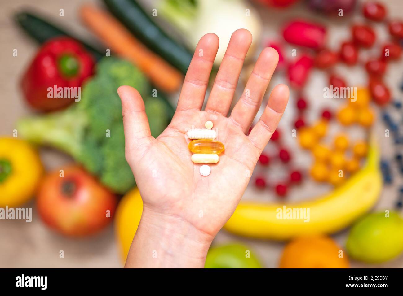Hand is holding food supplement tabletts over a wooden table full of ...