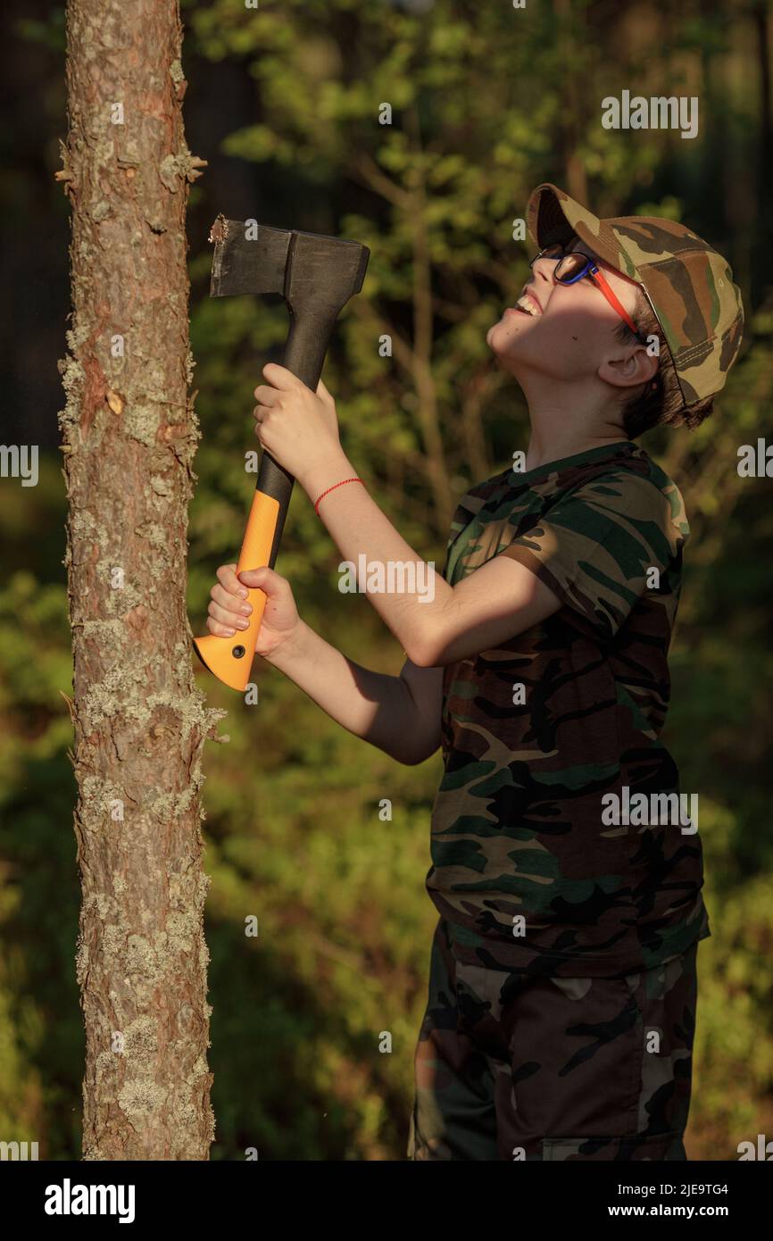 Boy in military clothes holding heavy axe. The concept of adventure ...
