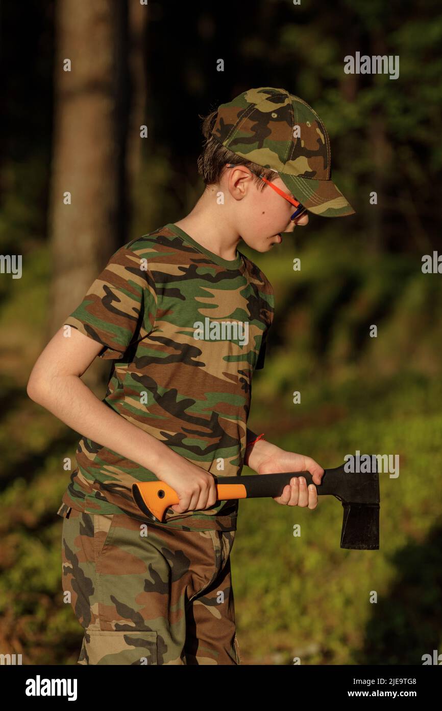 Boy in military clothes holding heavy axe. The concept of adventure ...