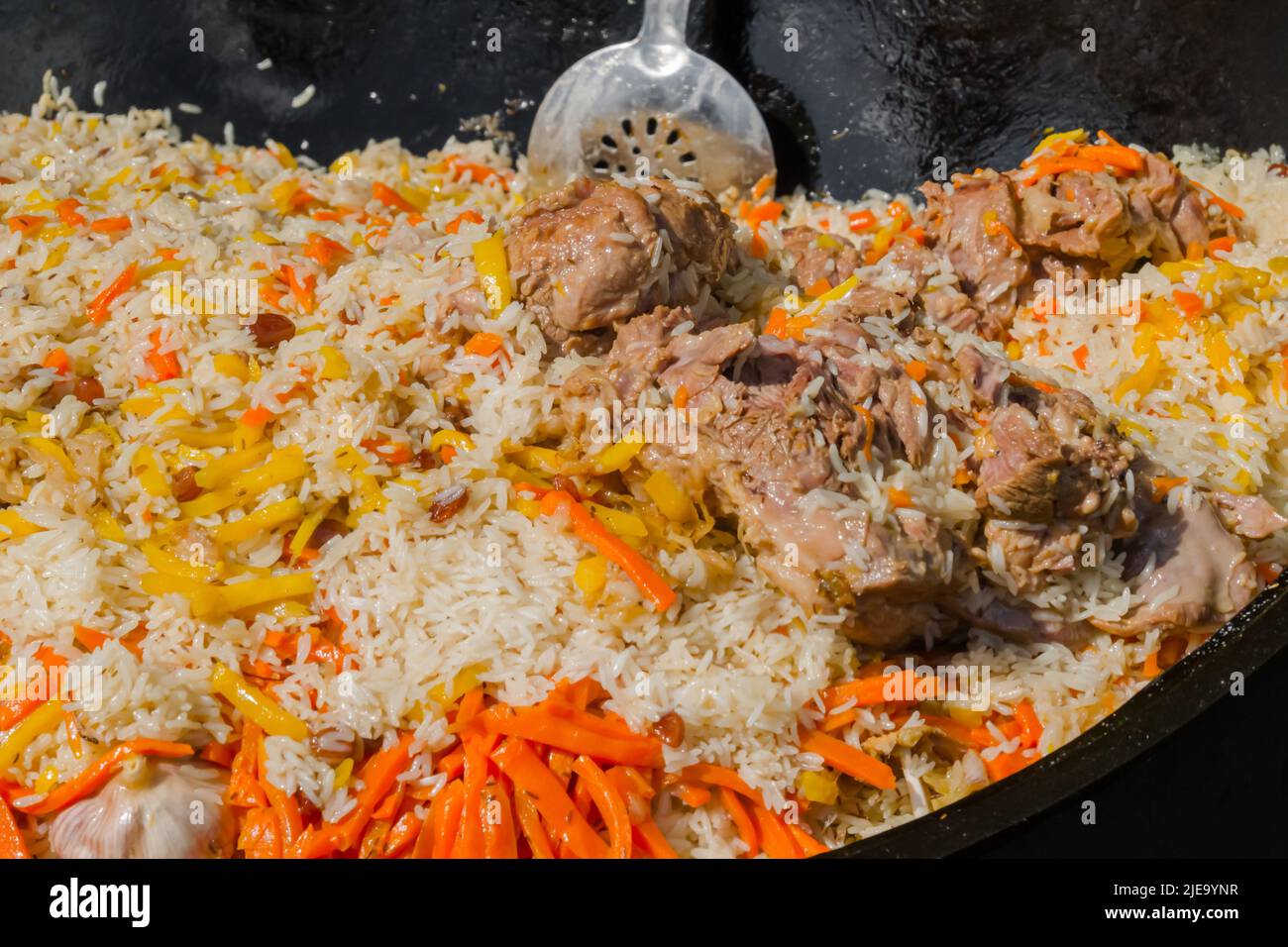 Process of cooking pilaf in huge cauldron at summer outdoor food market ...