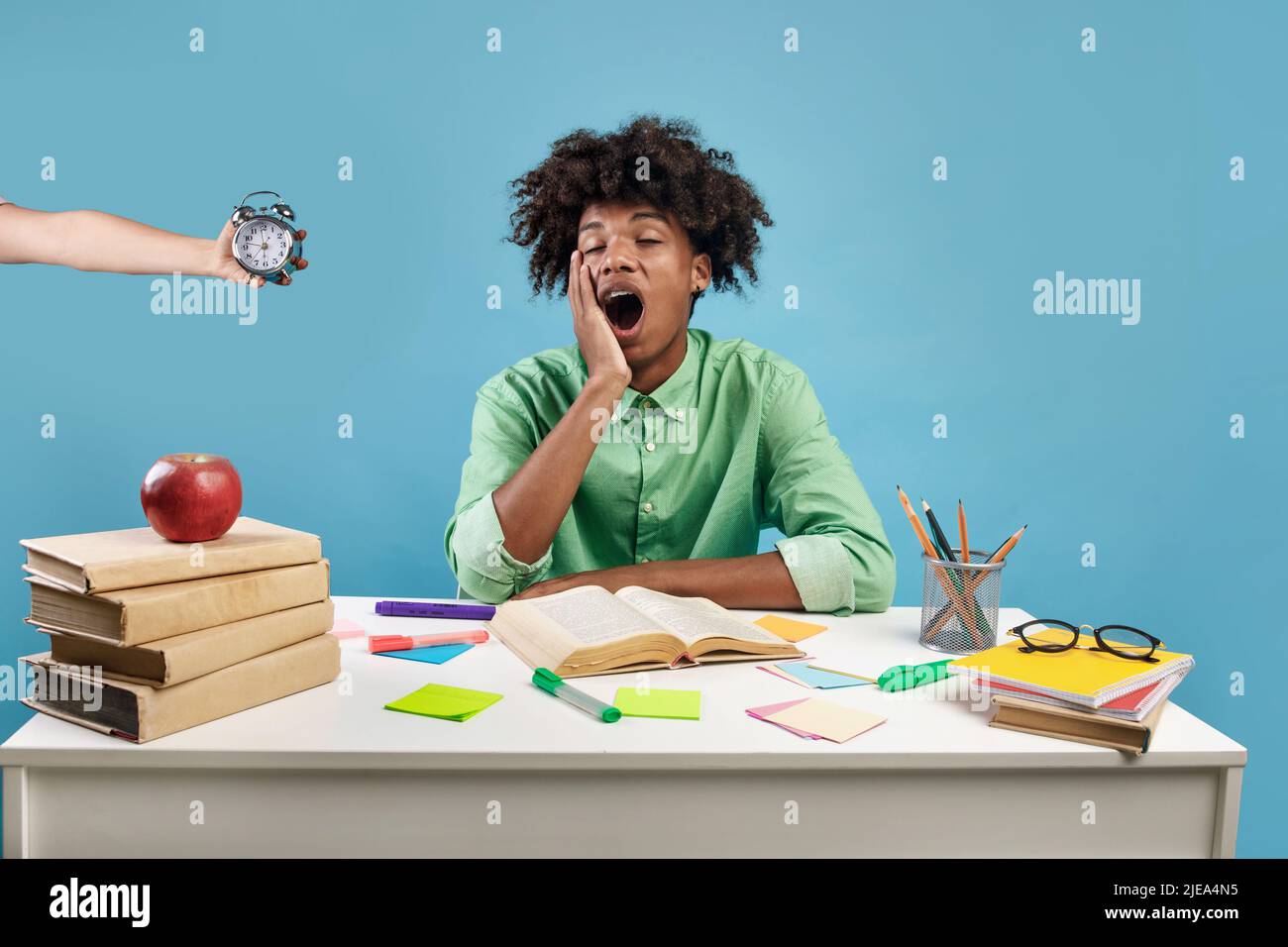 Tired african american male student yawning, sitting at desk with lot ...