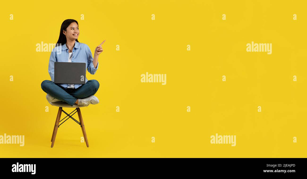 Smiling millennial asian lady sitting on chair and working on laptop ...