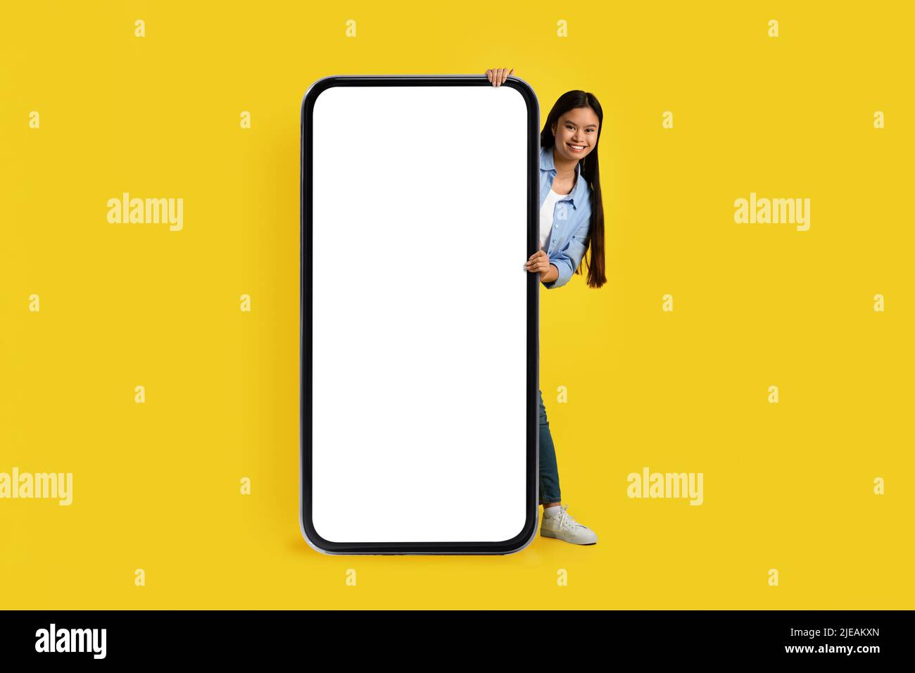 Glad funny young korean female peeking out from behind huge phone with ...