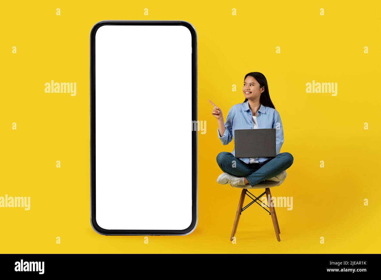Happy young japanese lady sit on chair with laptop pointing finger at ...