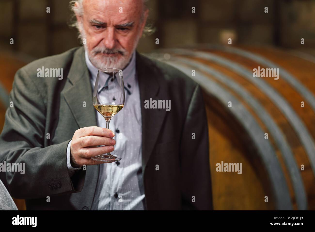 Caucasian senior man in a suit, standing in an old wine cellar with ...
