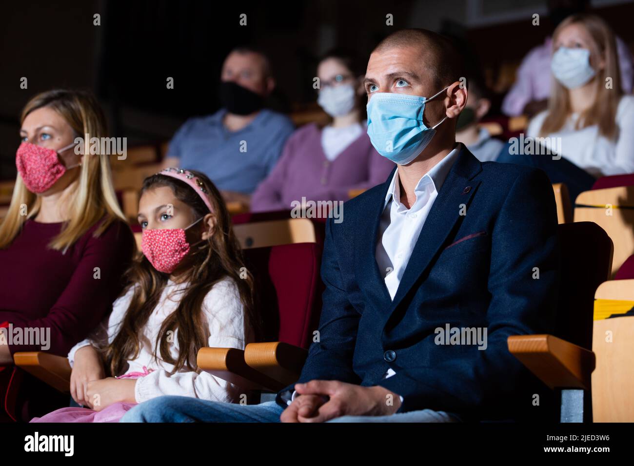 Family with child wearing protective masks eating popcorn and watching ...