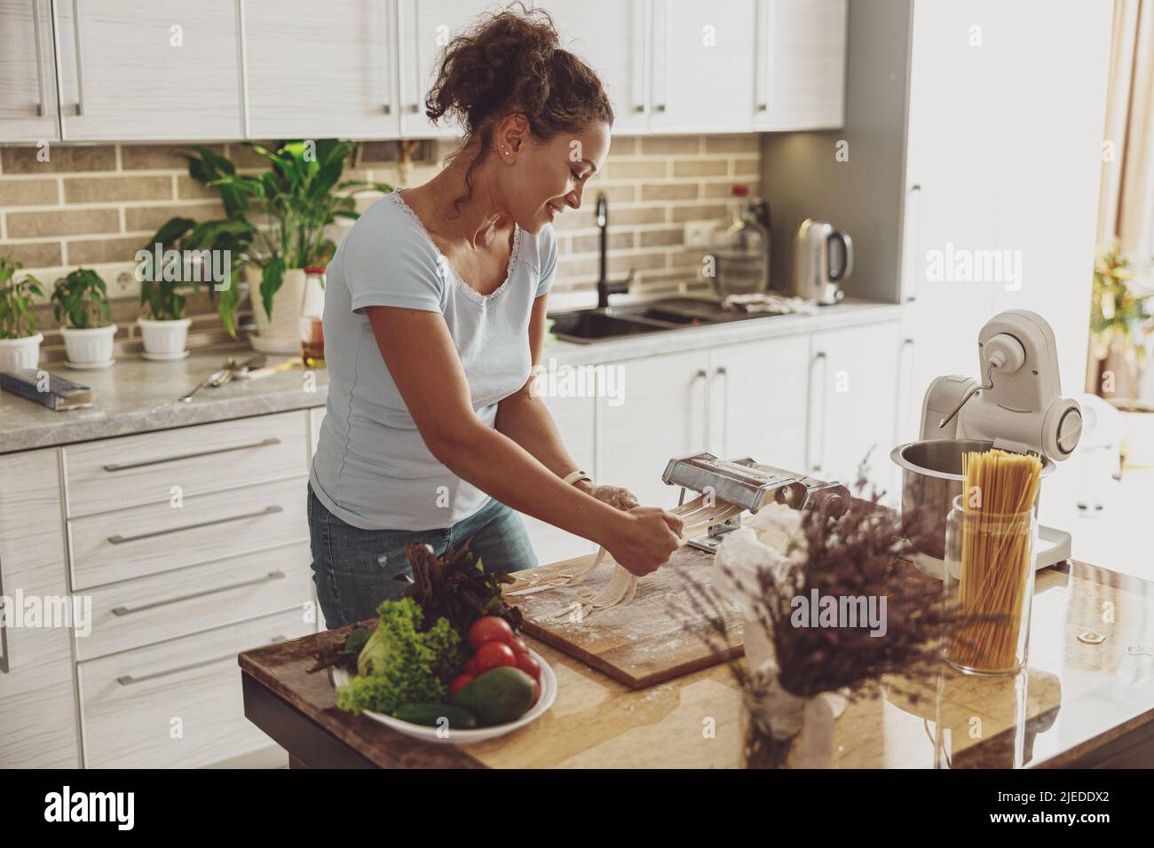 A satisfied woman standing in a modern kitchen near the table prepares ...