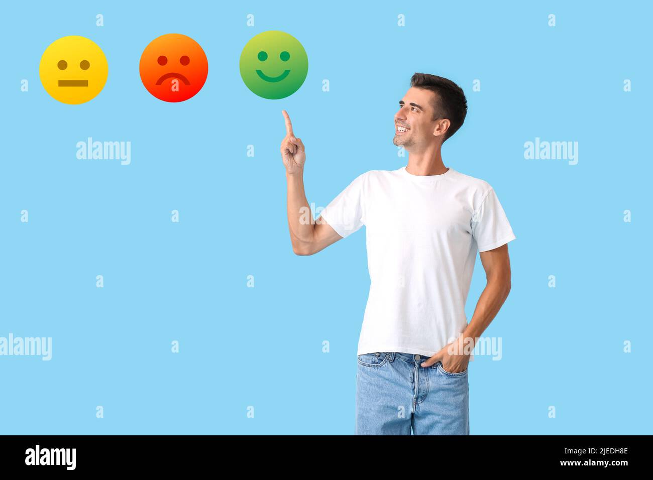 Handsome young man pointing at smiling emoticon on light blue ...