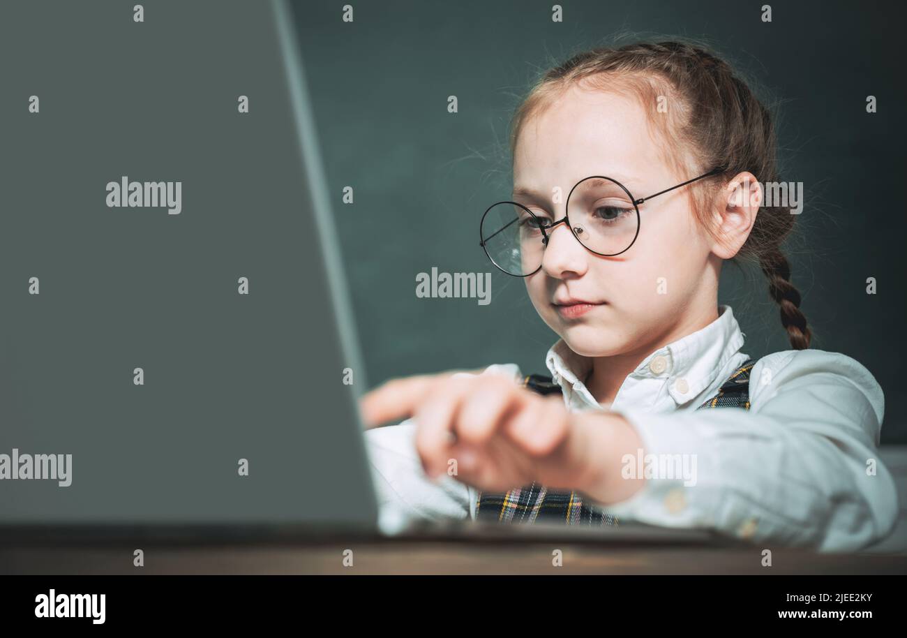Pupil working on laptop computer over blackboard background. Child near ...