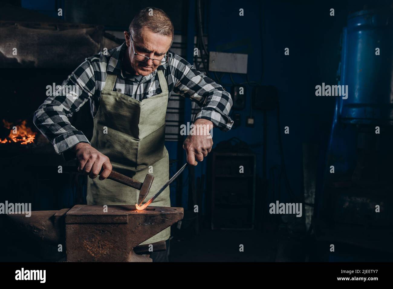 The blacksmith manually forging the red-hot metal on the anvil in ...