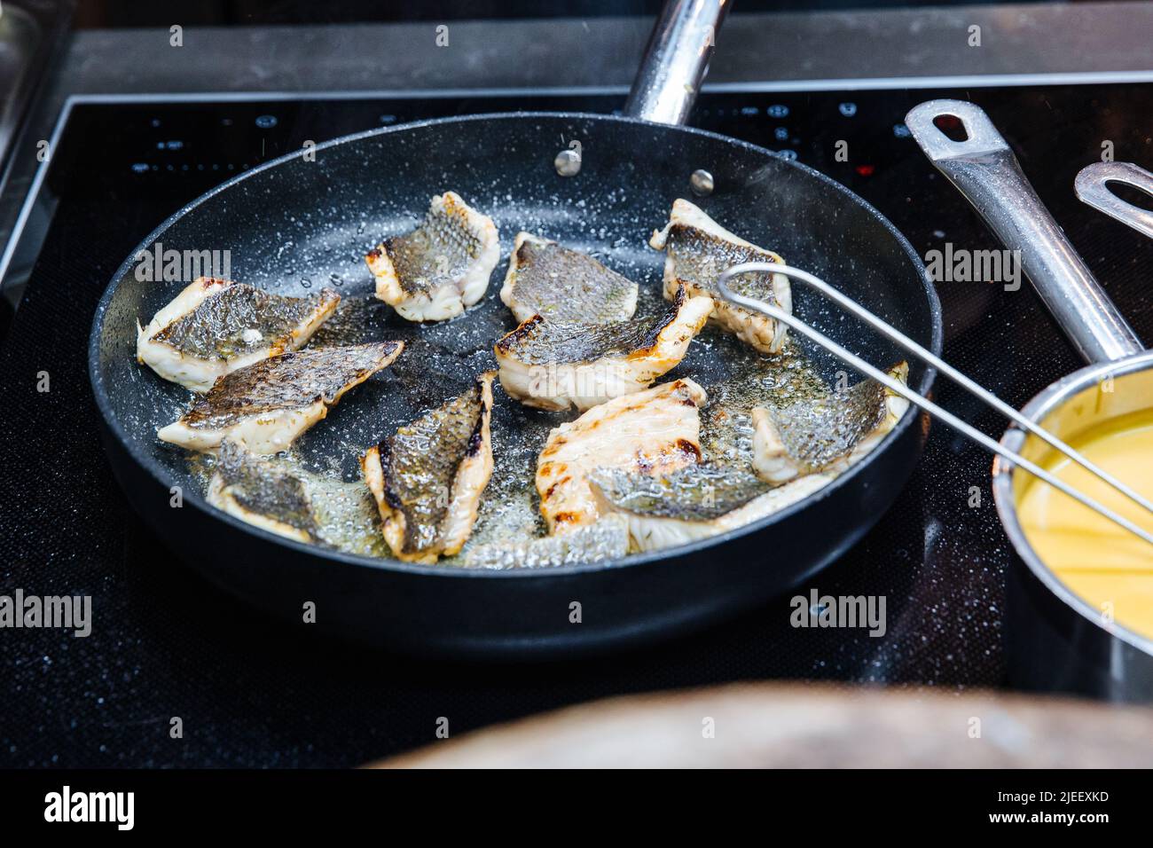 Pieces of fish cooking on a hot pan with olive oil on a stove. Dinner ...