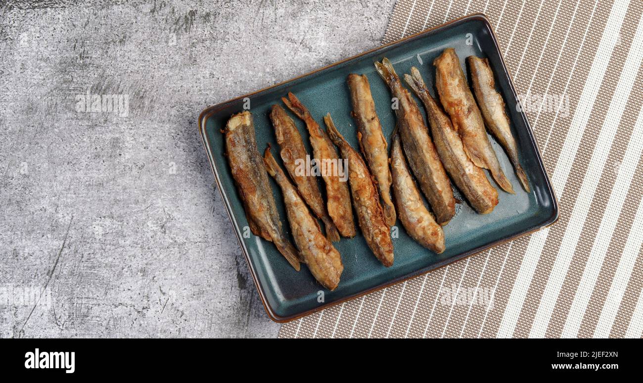 Pan fried capelin or smelt on a rectangular plate on a dark background ...