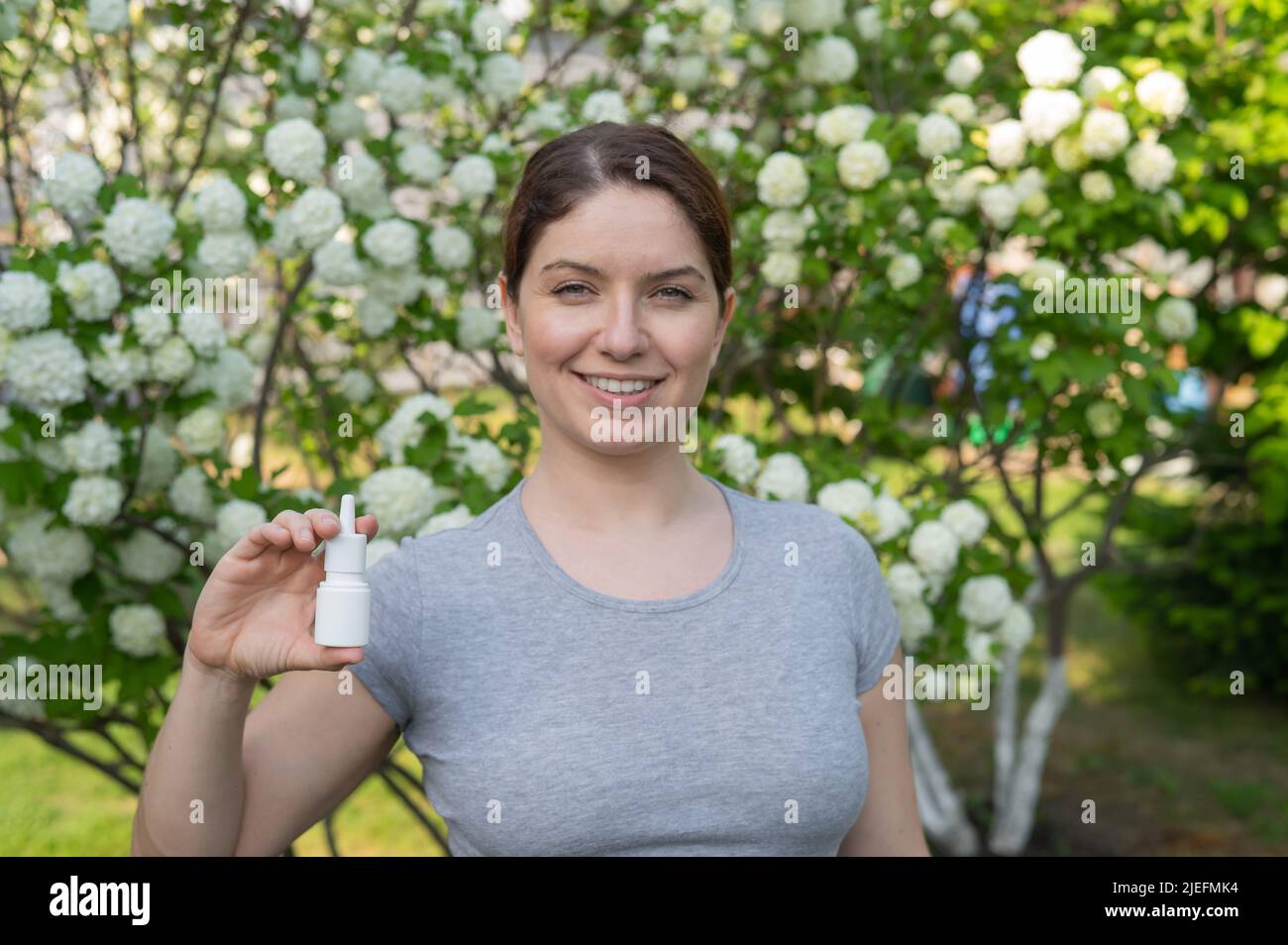 Happy woman demonstrating nasal spray on the background of a blossoming ...