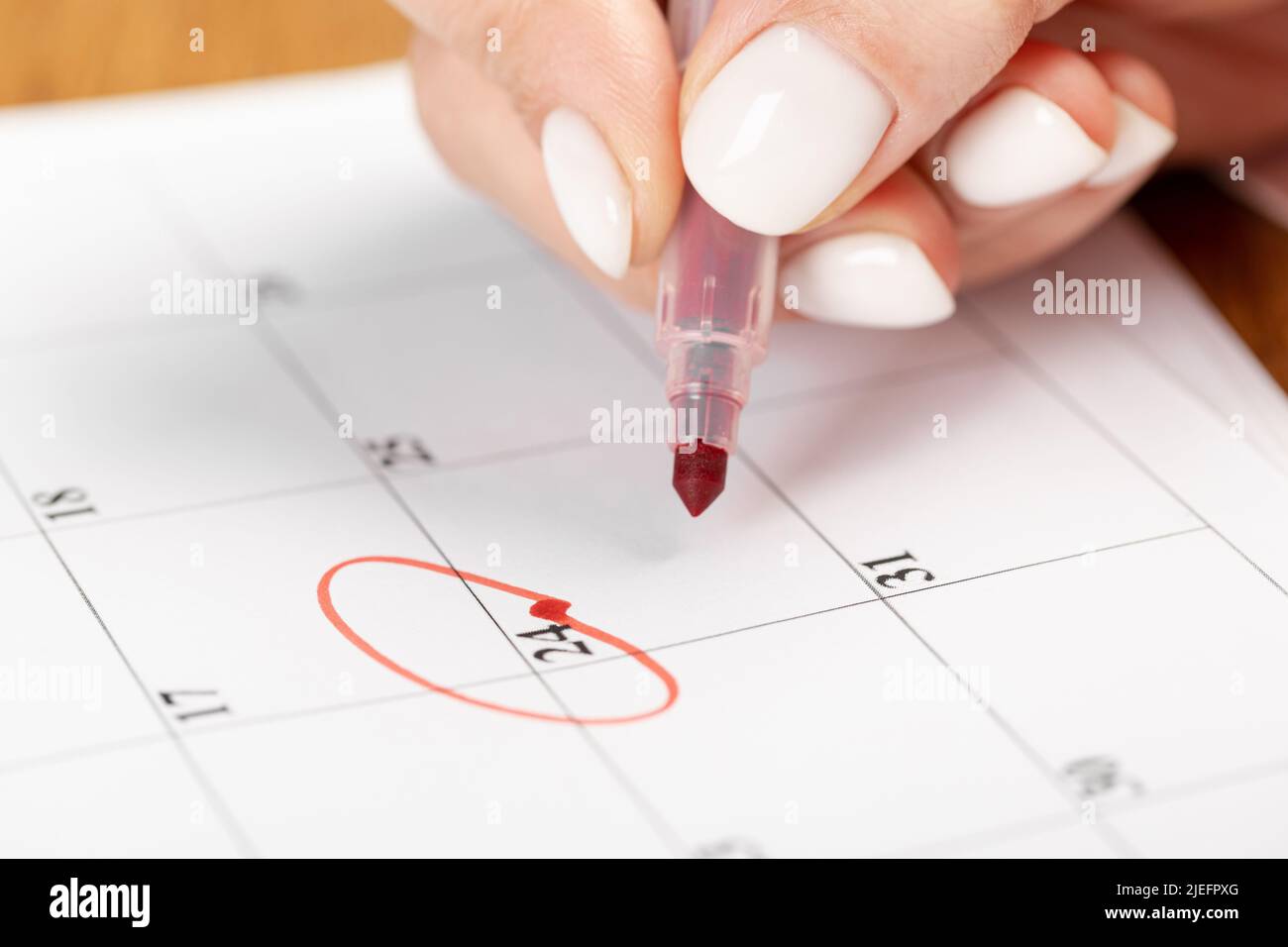female hand marking with a red pen on a calendar circles the day ...