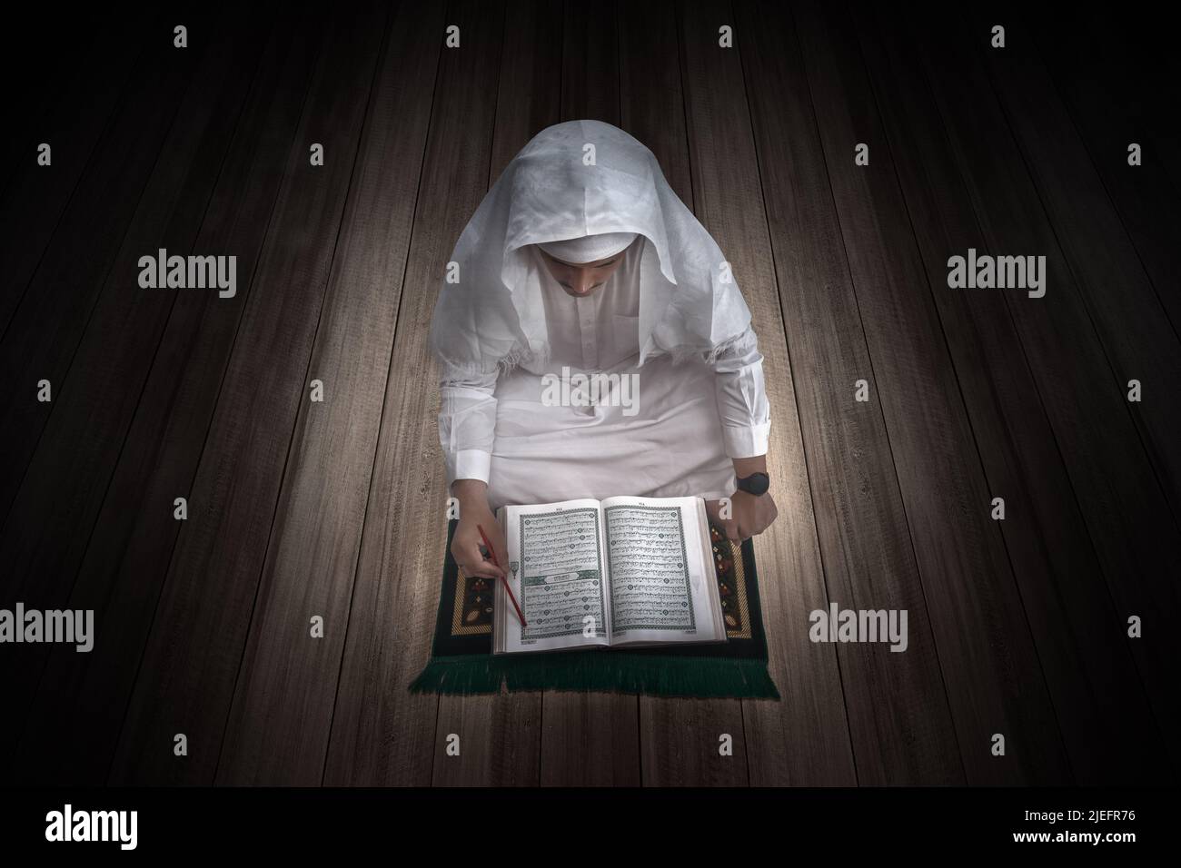 Arab Muslim man sitting and reading the Quran on the prayer rug with a ...