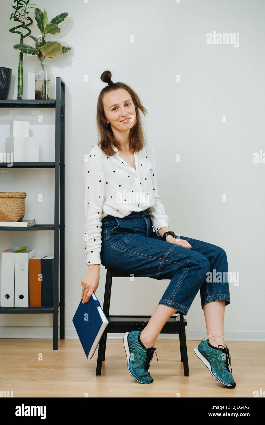 Smiling woman sitting sideways on a stool at home looking at the camera ...