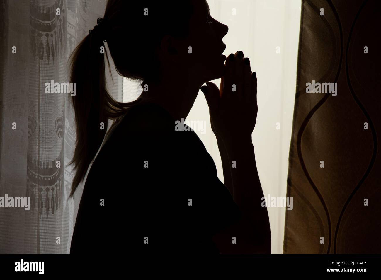 Ukrainian girl pray near the window in the dark to God for salvation ...