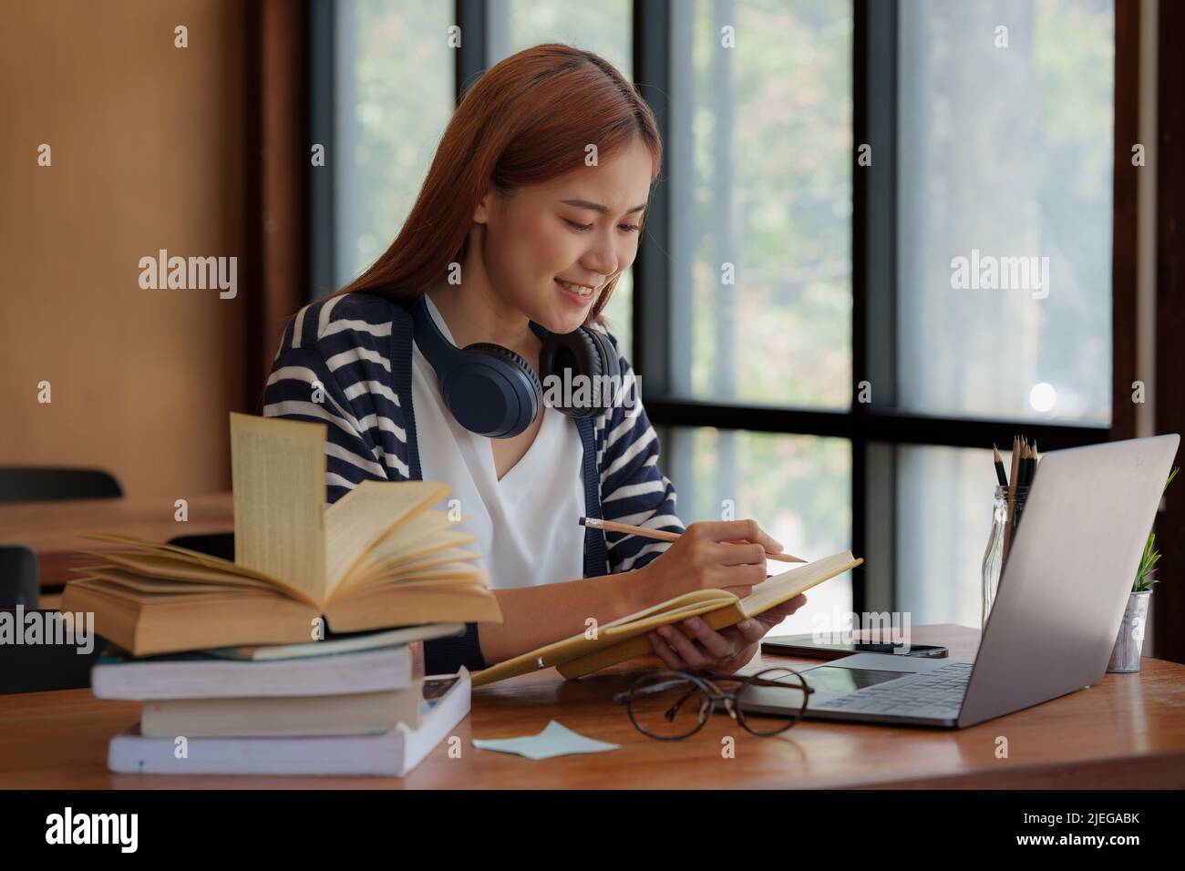 Young asian girl student wear headphone and writing a notebook and ...