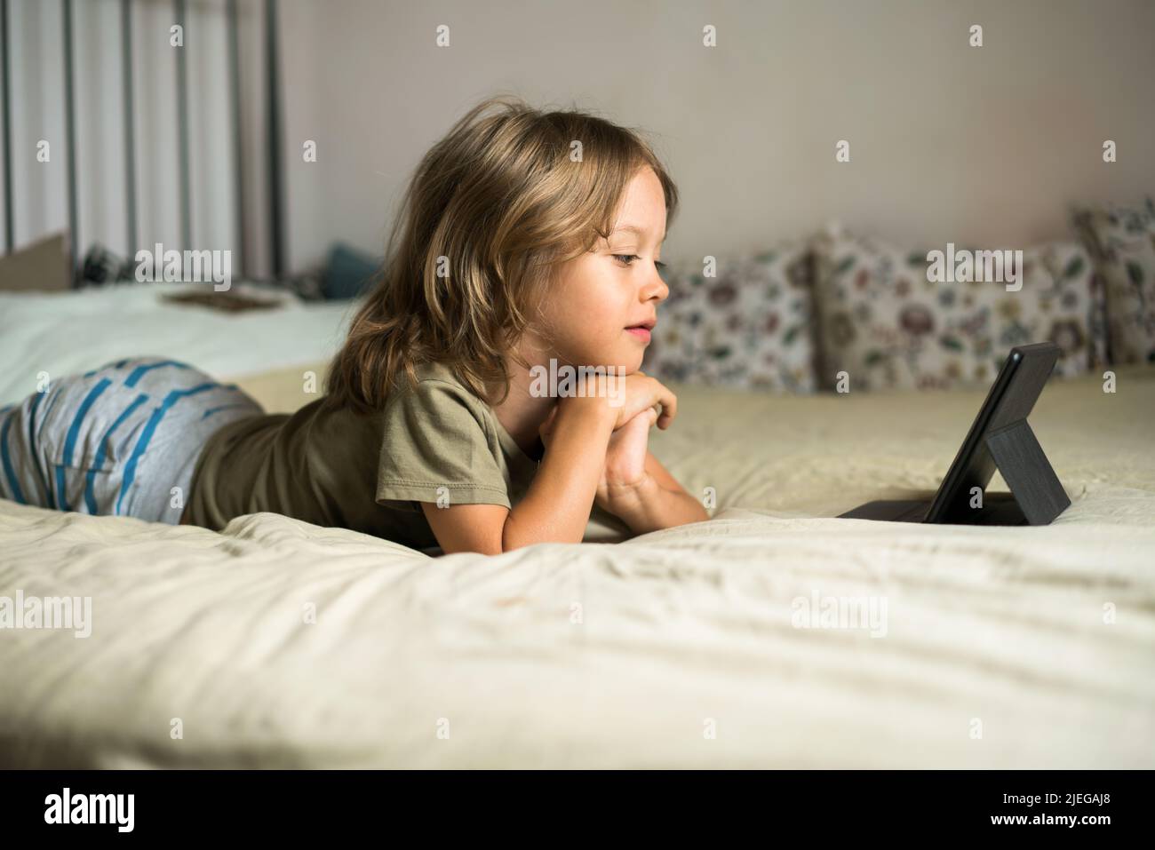 Boy lying on the bed using digital tablet computer playing games or ...