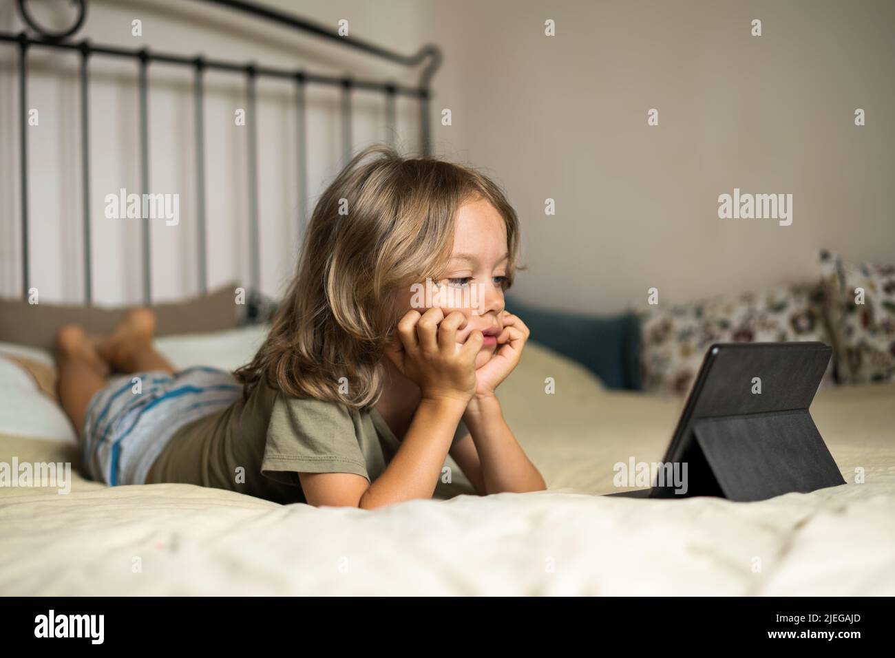 Boy lying on the bed using digital tablet computer playing games or ...
