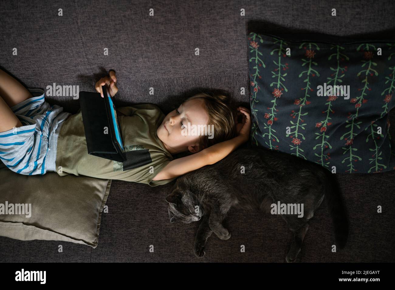 Boy lying on sofa using digital tablet computer playing games or ...