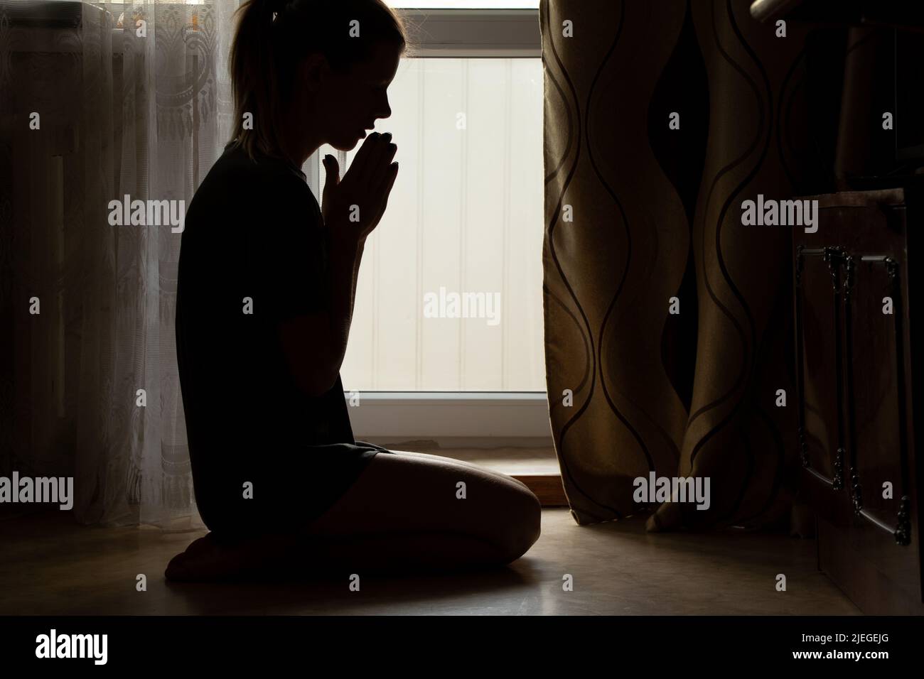 Ukrainian girl pray near the window in the dark to God for salvation ...