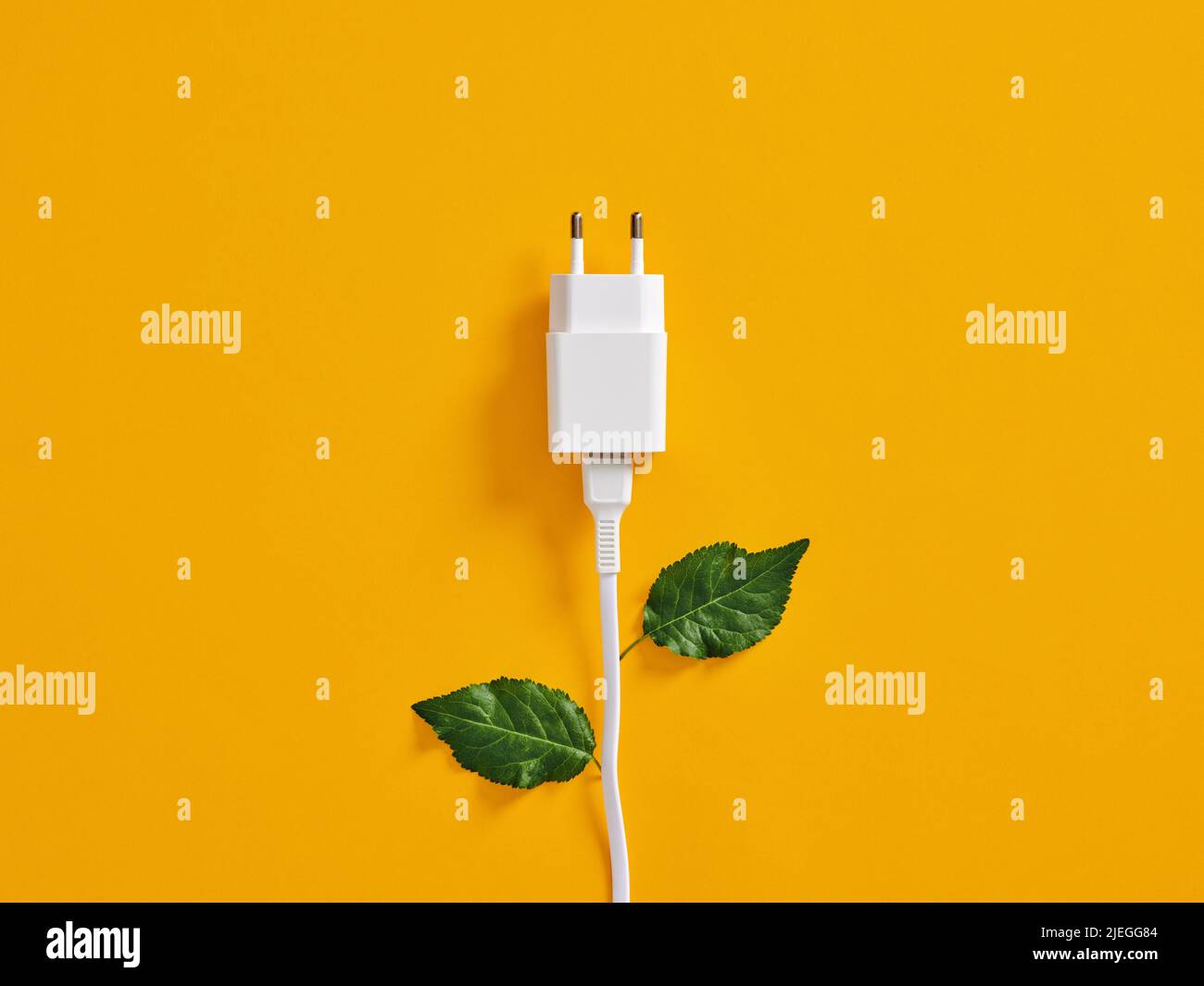 White electric plug with green leaves on yellow background. Eco ...