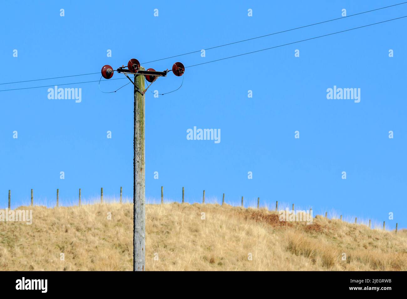 Electricity cables fixed to a wooden poll with a blue sky background ...
