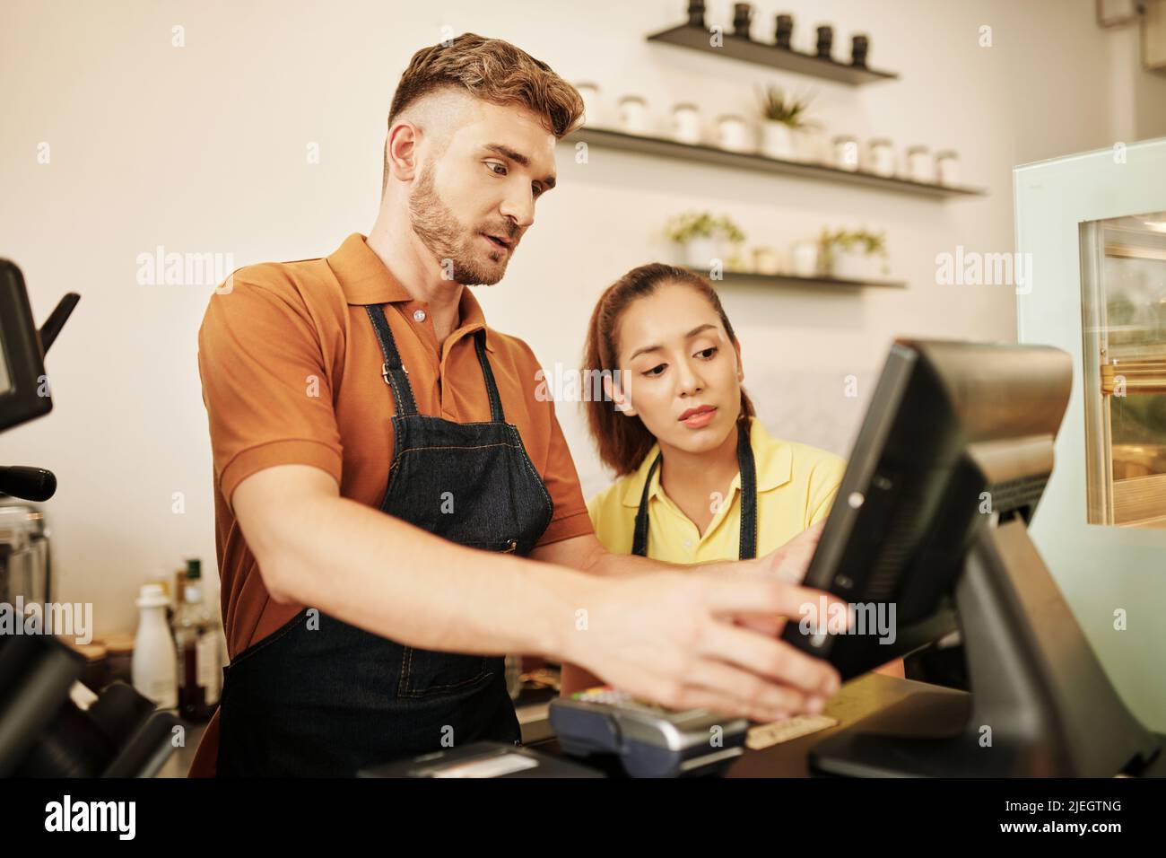 Coffeeshop barista explaining new worker how to use cash register Stock ...