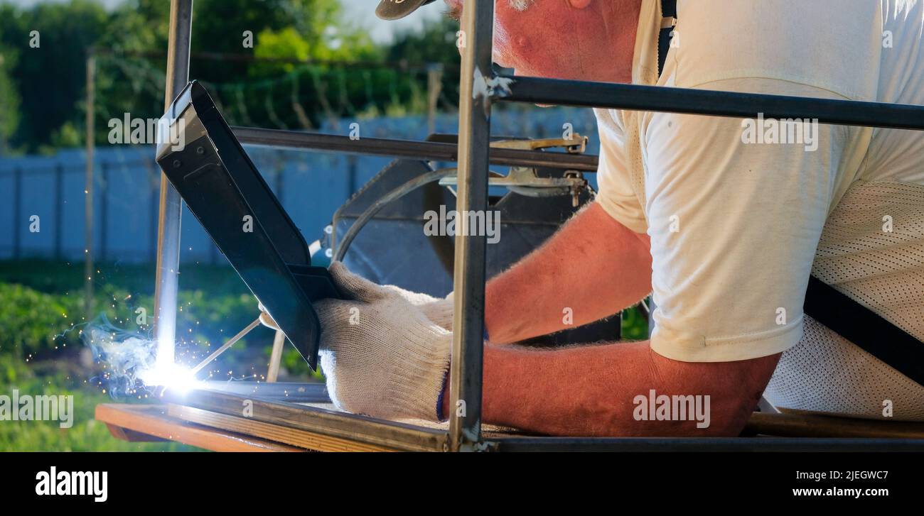 An elderly male welder welds metal with electric arc welding. Selective ...