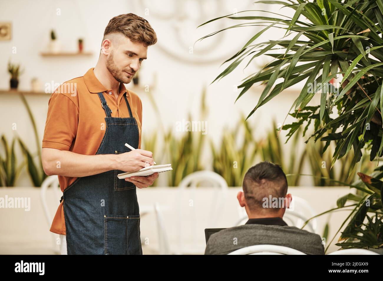 Coffeeshop waiter talking to customer and writing down order details ...