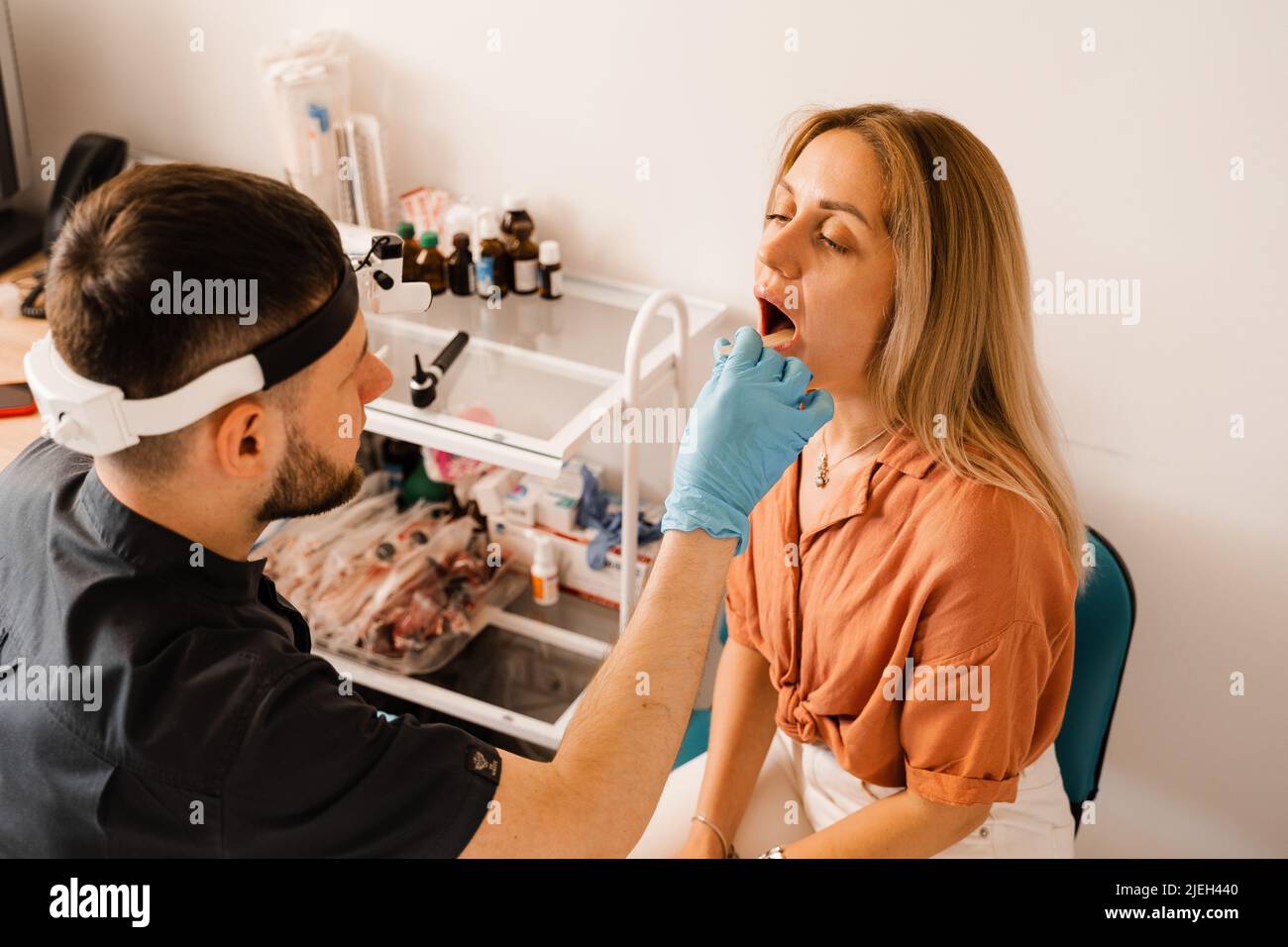 Oropharyngoscopy procedure. Otolaryngologist examines woman throat with ...